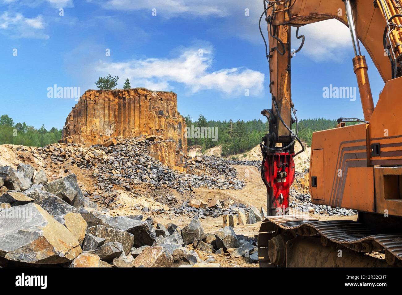 Excavators in a basalt quarry near the forest. Large orange excavator ...