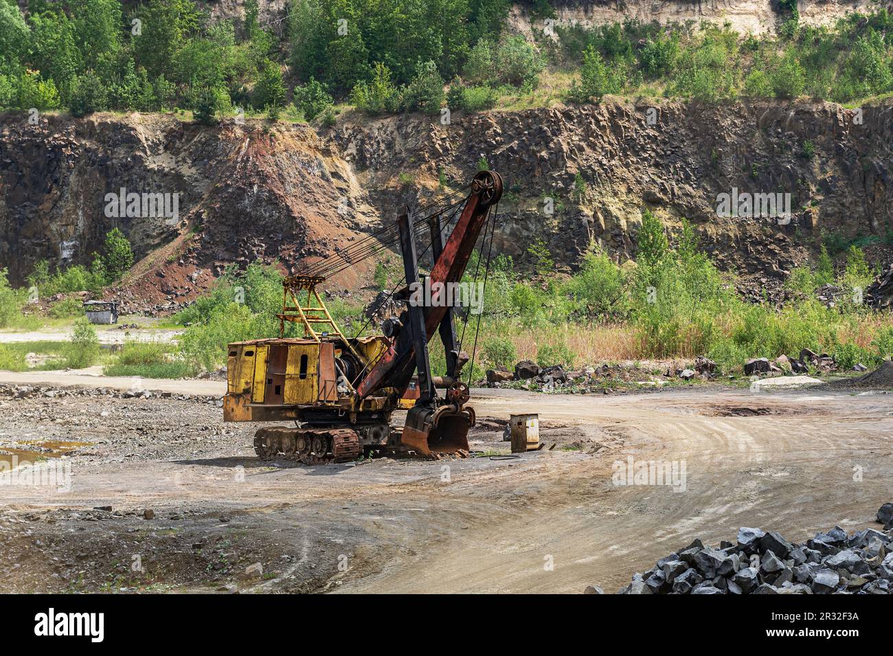 Excavators in a basalt quarry near the forest. Large orange excavator ...