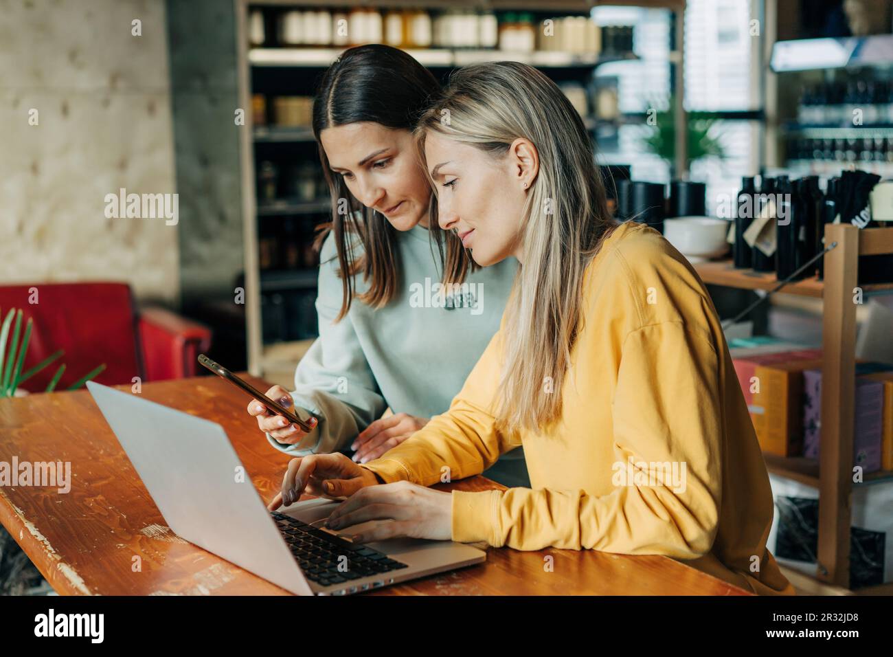 Two business women work behind the counter using electronic gadgets ...