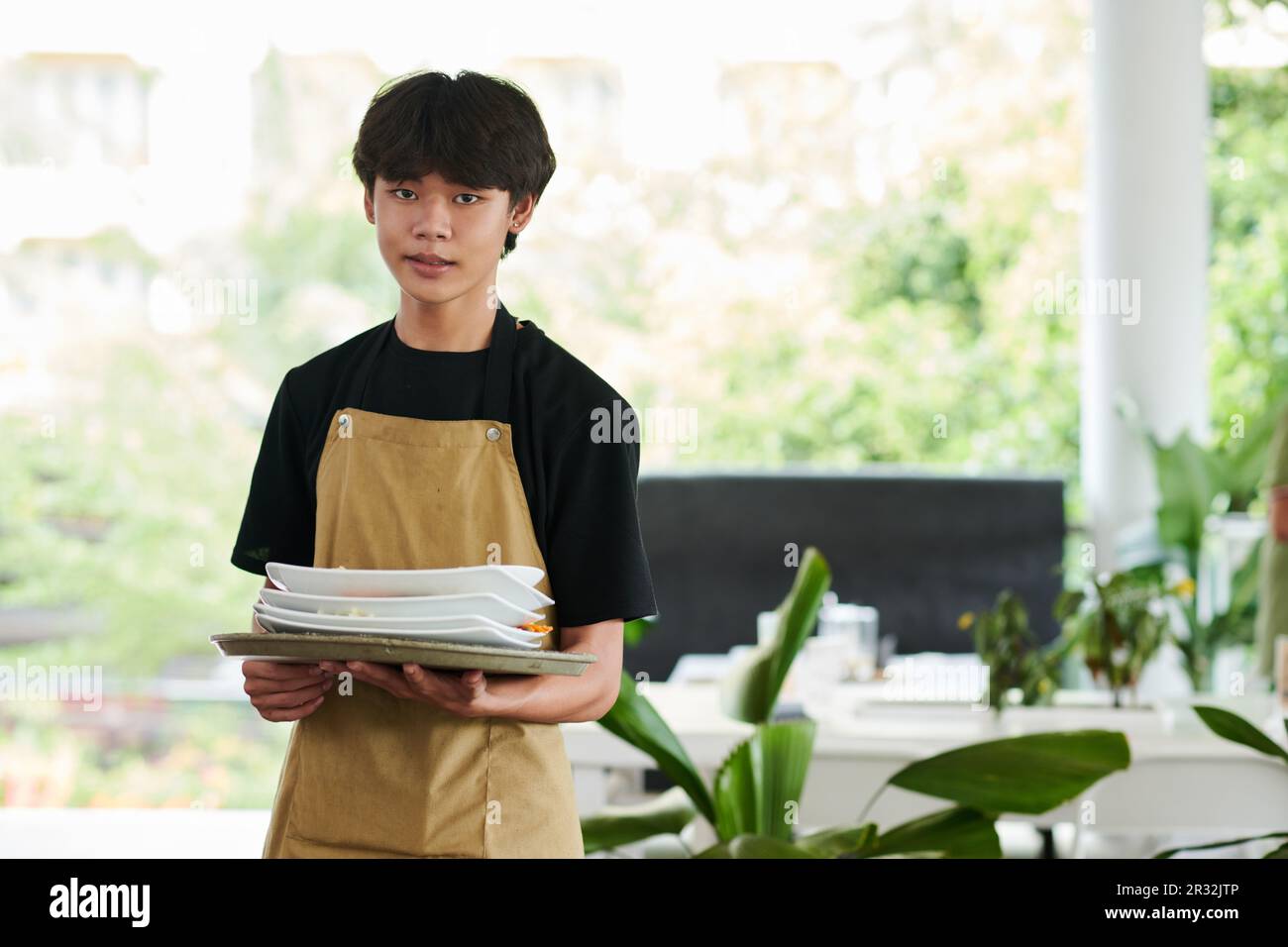 Restaurant waiter holding pile of dirty plates he collected on tables ...