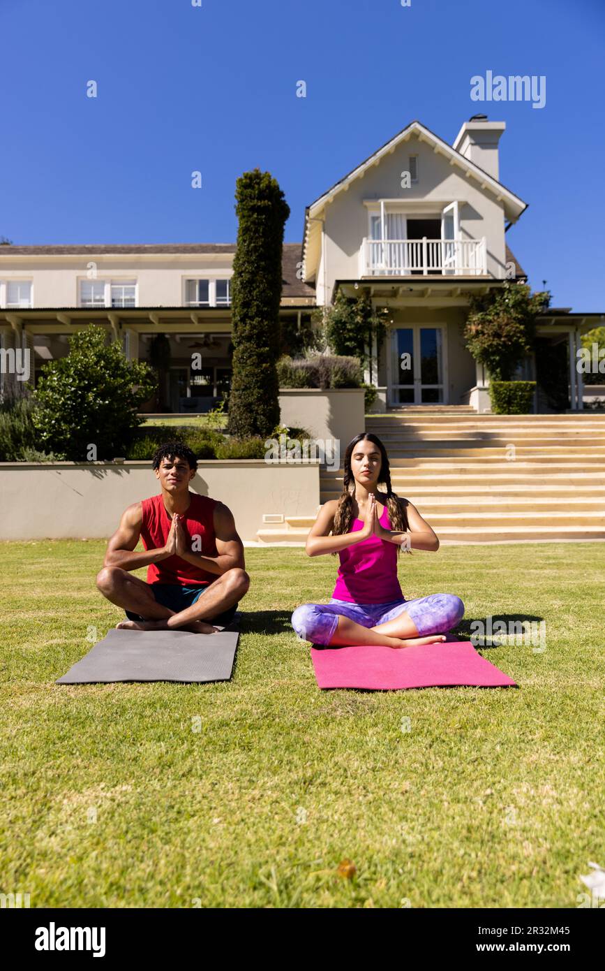 Happy diverse fit couple practicing yoga meditation sitting in sunny garden, with copy space ...