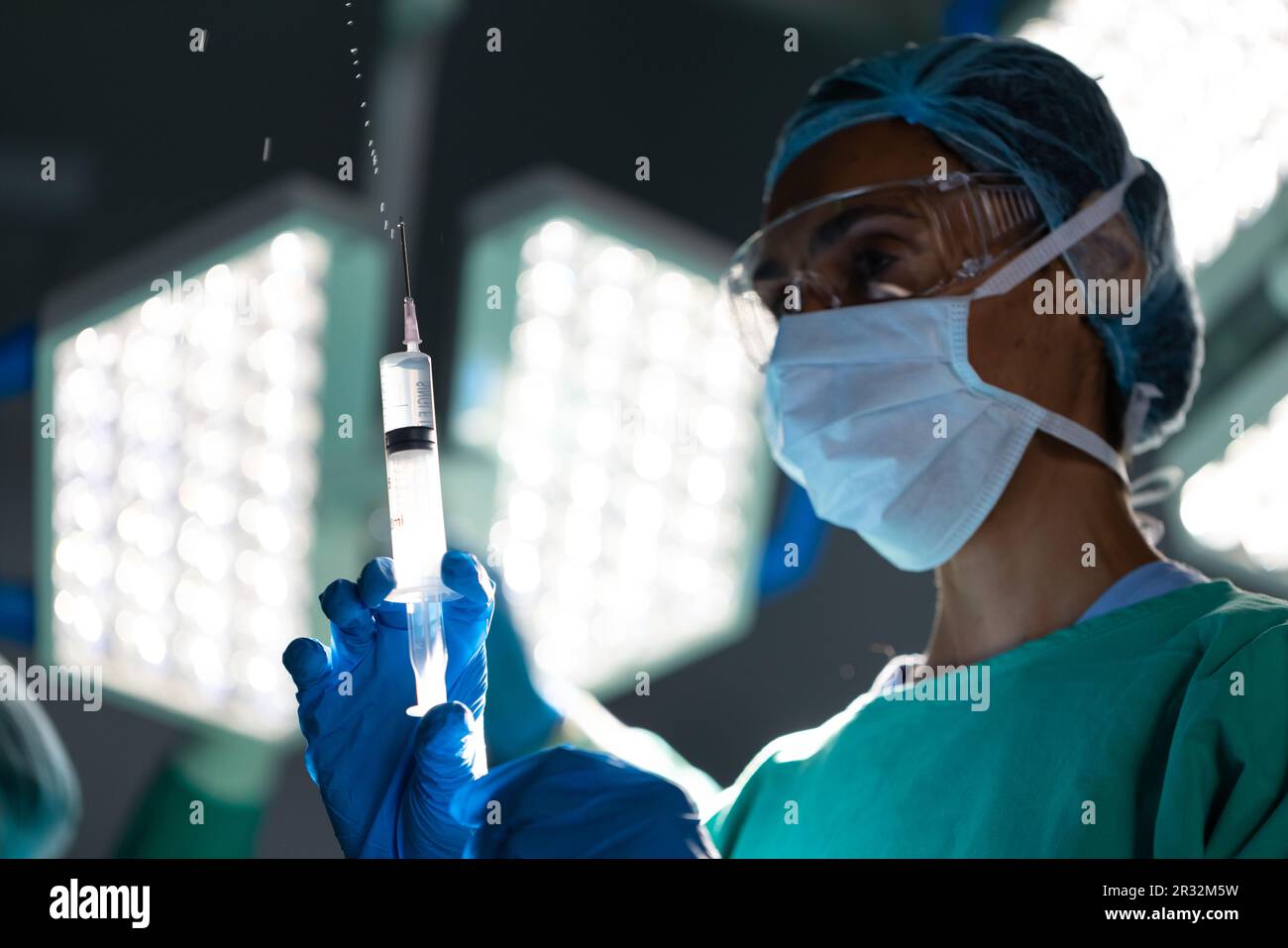 Biracial female surgeon preparing syringe in operating theatre at ...