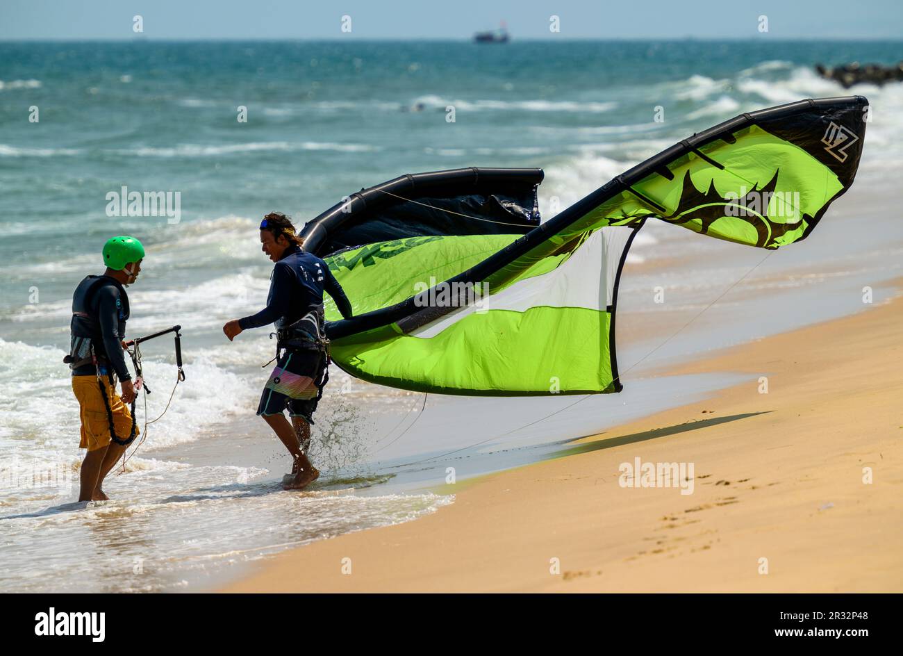 A kitesurfer helps another with the kite gear on the beach in Mui Ne ...