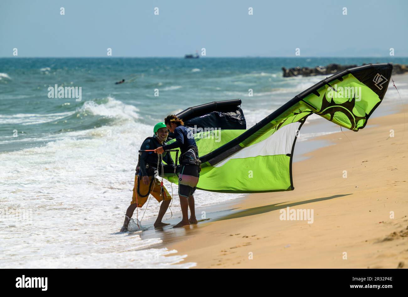 A kitesurfer helps another with the kite gear on the beach in Mui Ne ...