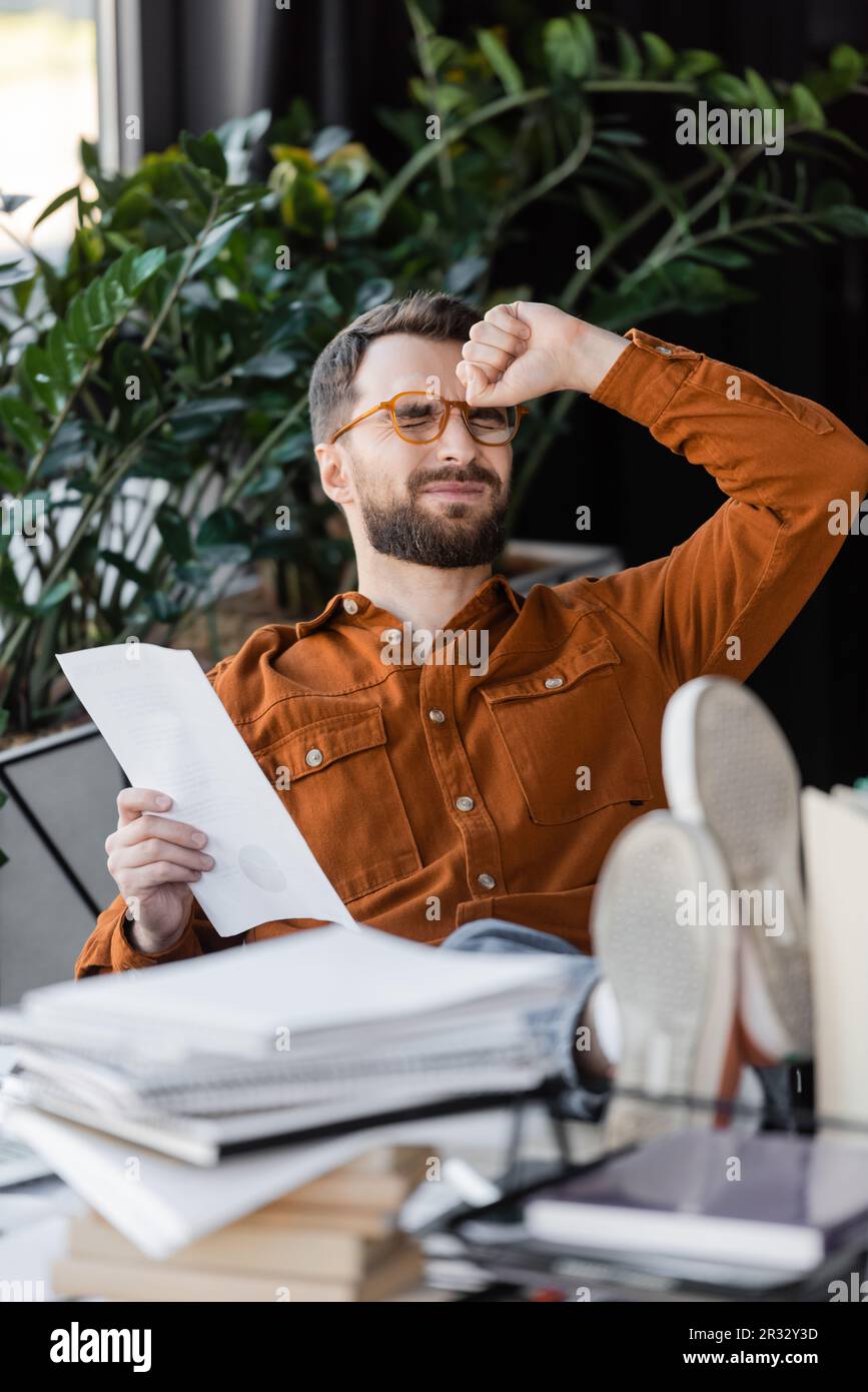 busy and tired businessman in eyeglasses and shirt holding document ...