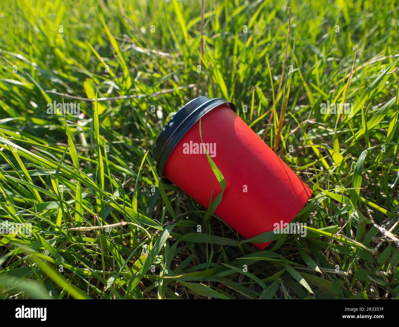 Used red paper disposable water coffee tea cup thrown on a grass lawn ...