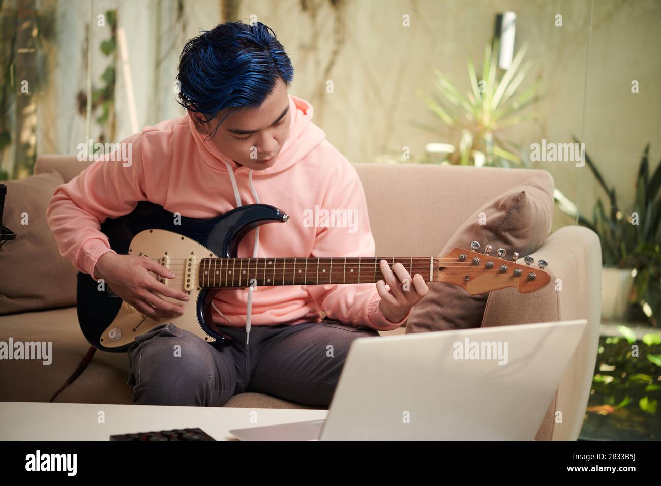 Young man following tutorial on laptop when learning playing guitar at ...