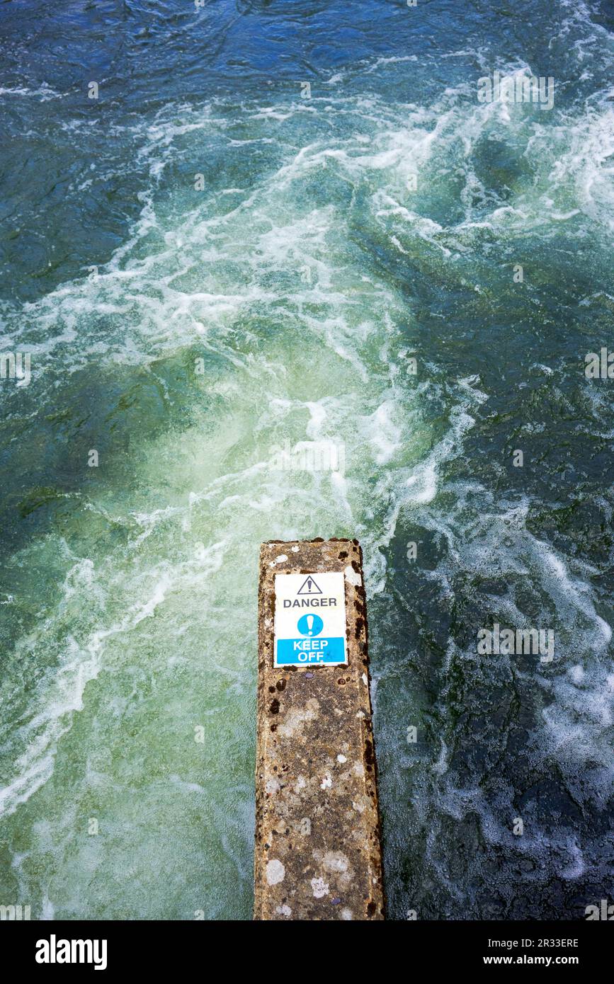 Water rushing past a concrete pier with a danger keep off sign Stock ...