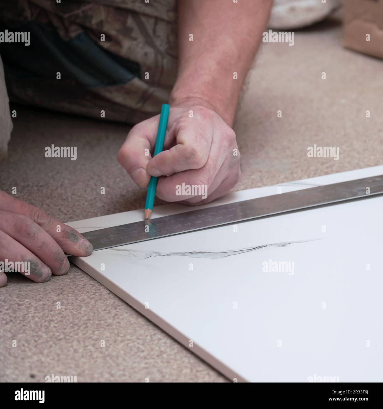 The hands of a man marking ceramic floor tiles with a ruler and pencil ...