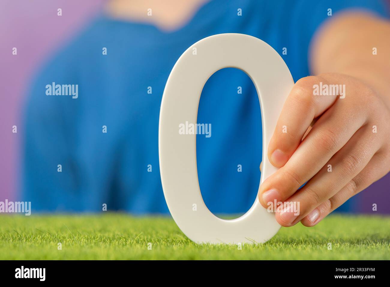 Number 0 in hand. Hand holding white number zero over green grass and ...
