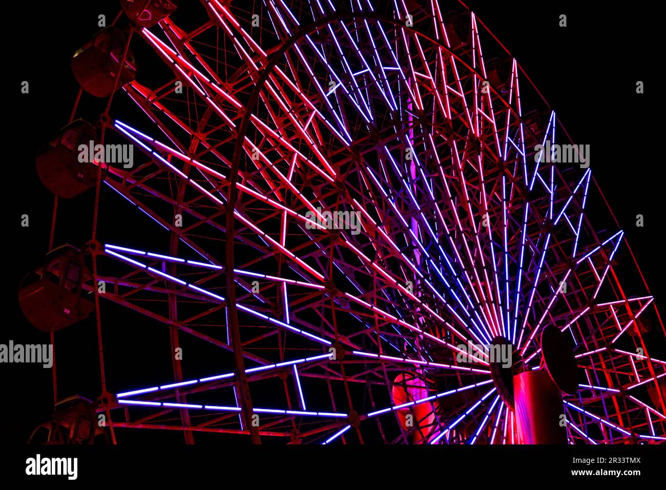 Red and purple light fluorescent on structure of ferris wheel with dark ...