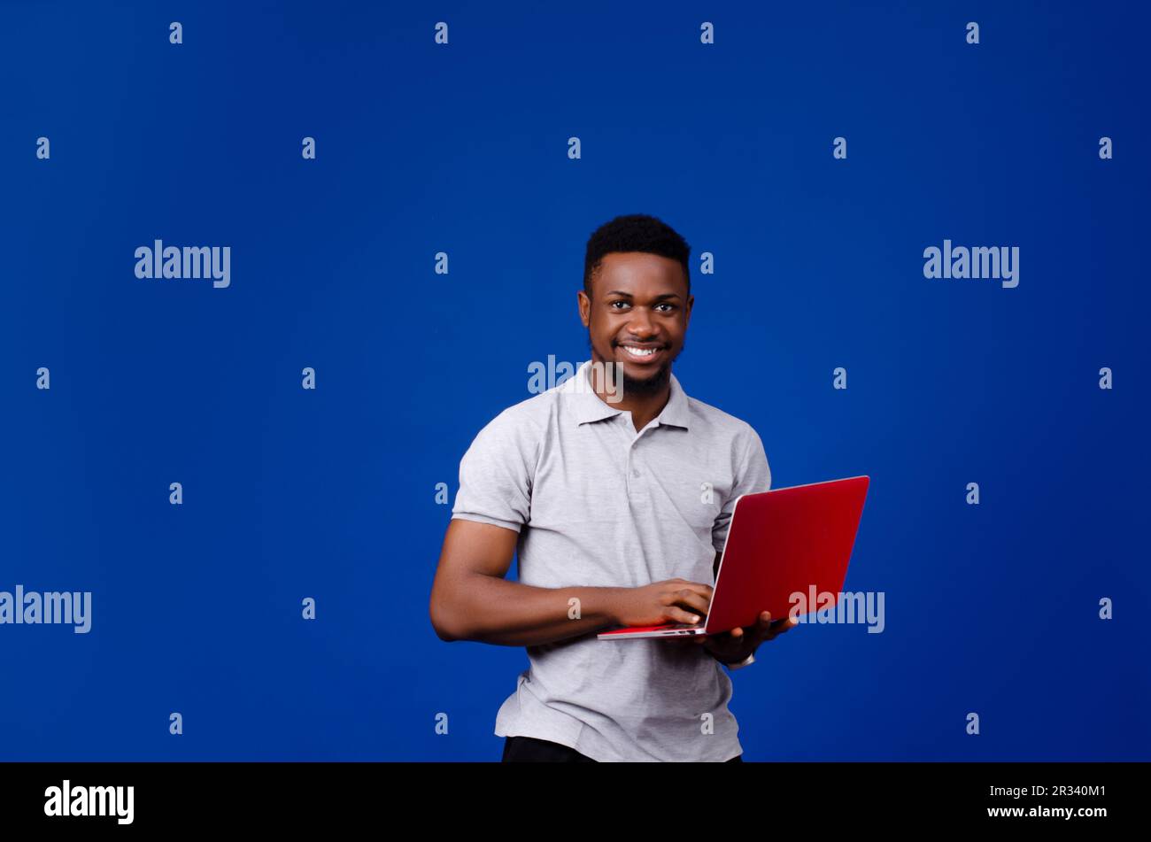 Young African man standing and smiling while working on a laptop, on a ...