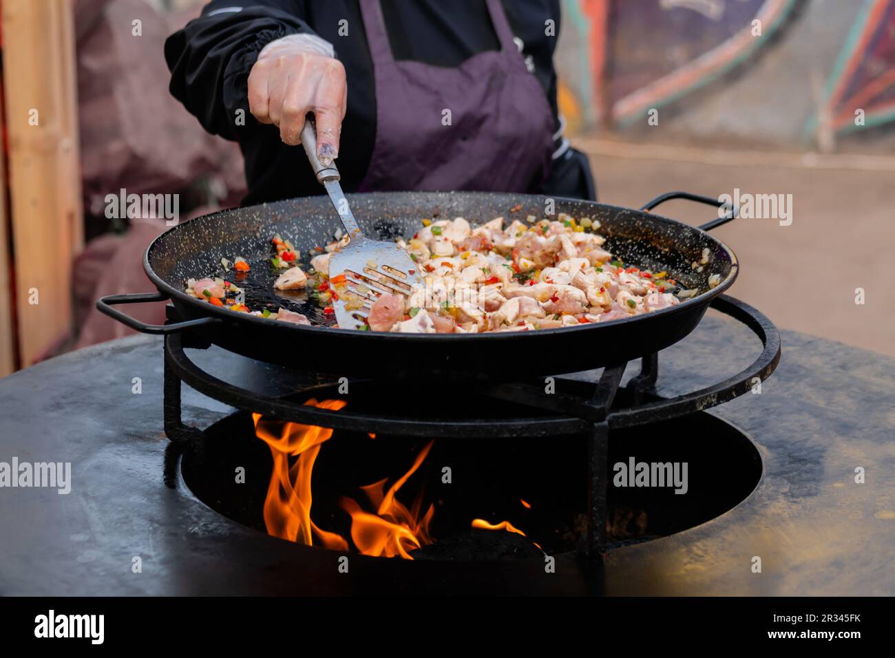 Woman chef cooking paella - fried chicken meat pieces, peppers, peas in ...