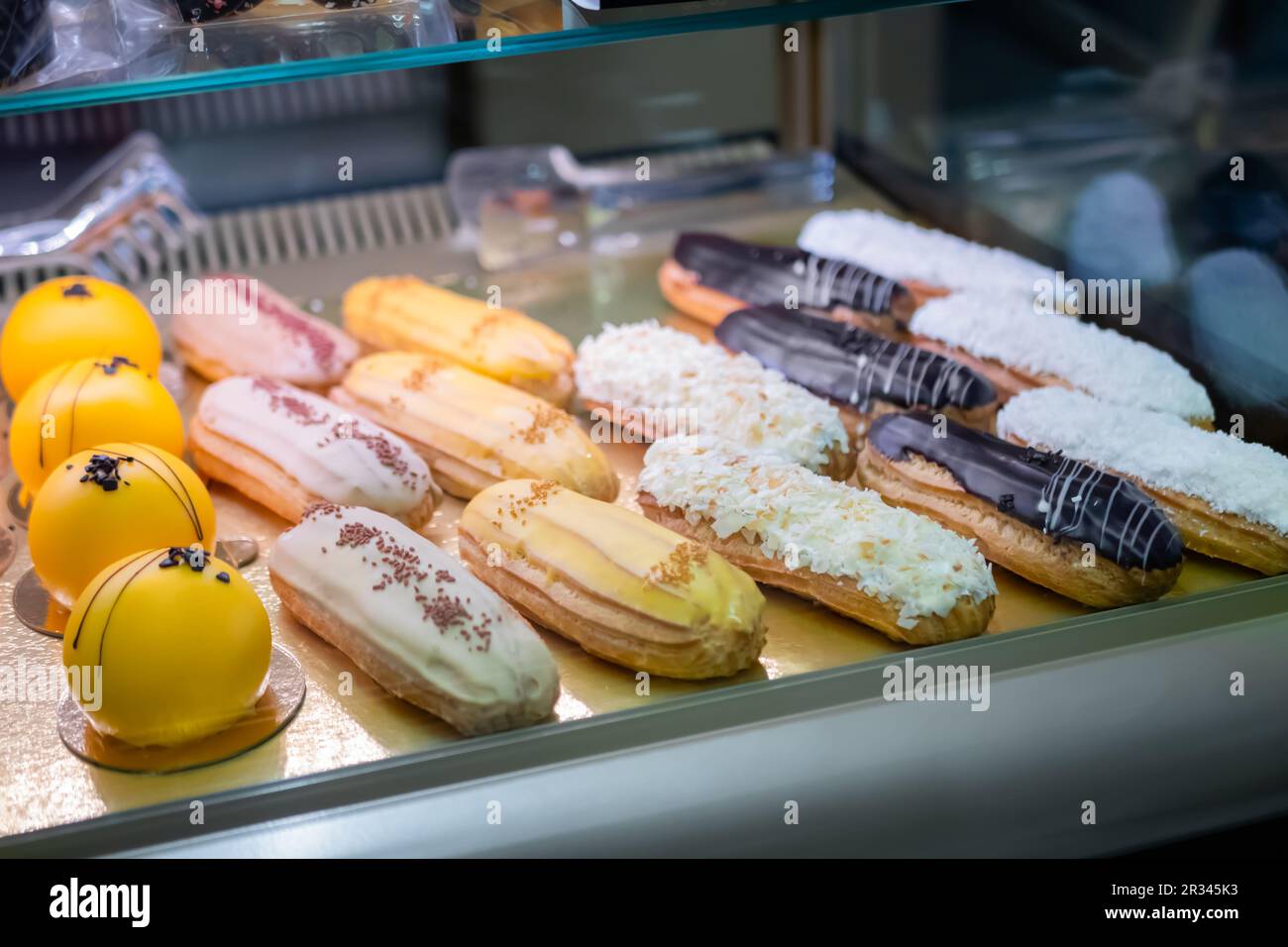 Set of multicolor mousse cakes and eclairs on counter at food market ...