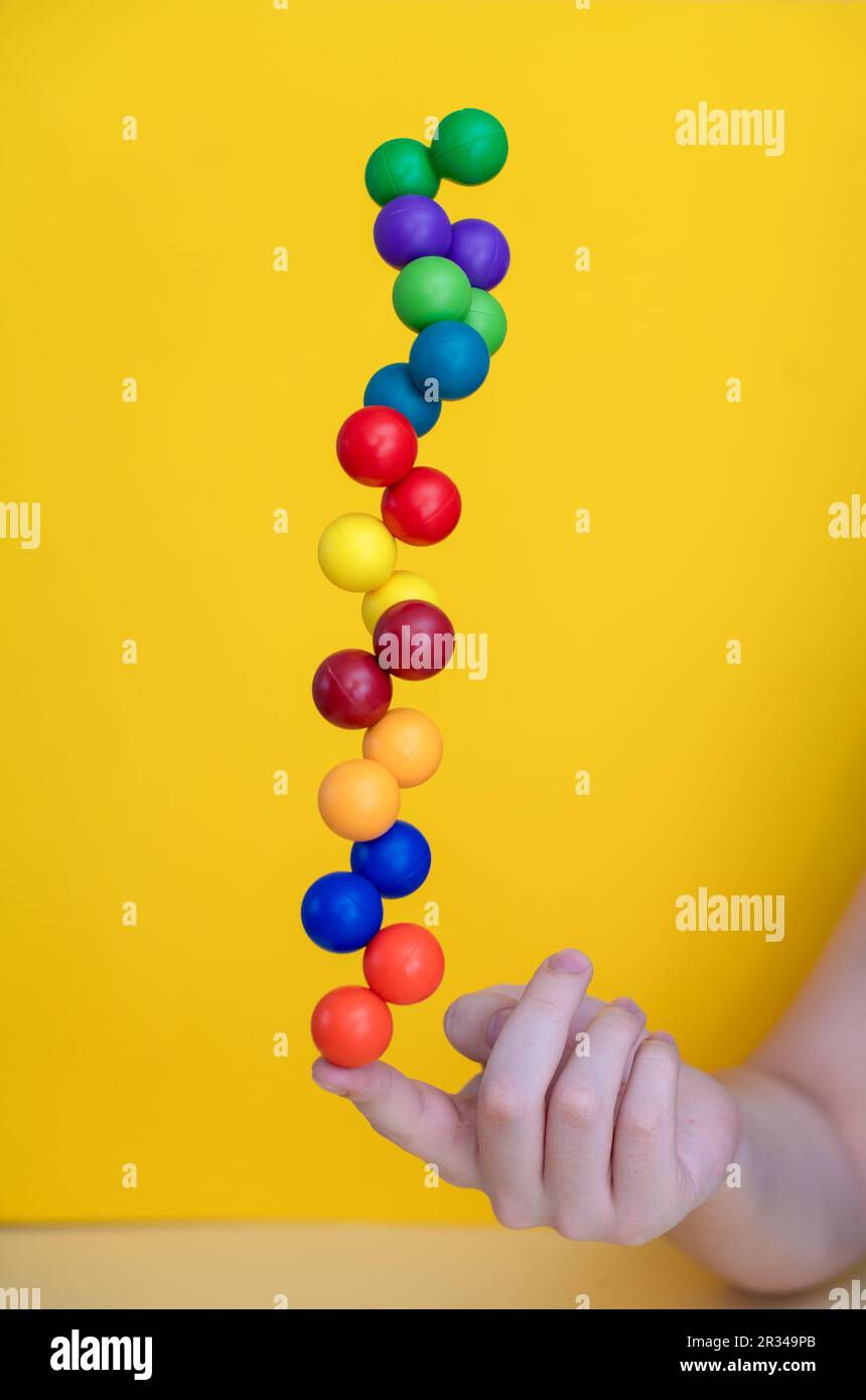 Balancing colored plastic balls on a finger on a yellow background ...