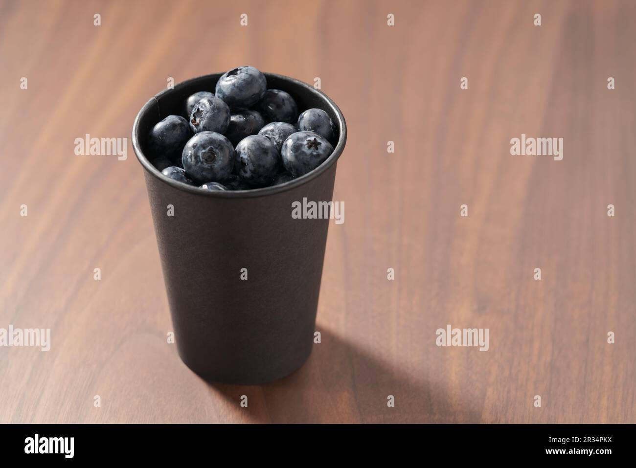 Blueberries in black paper cup on walnut table, shallow focus Stock ...