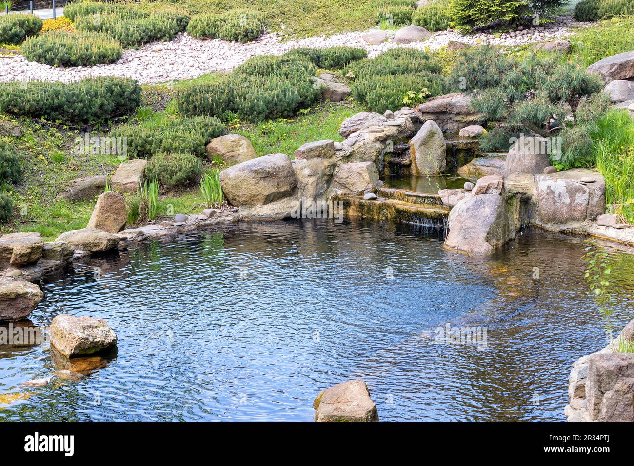The stream flows into a garden pond bordered by stone boulders around ...