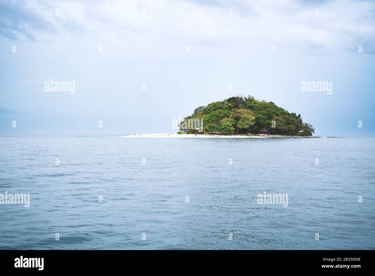 Small remote white beach island with lush green trees in light blue ...