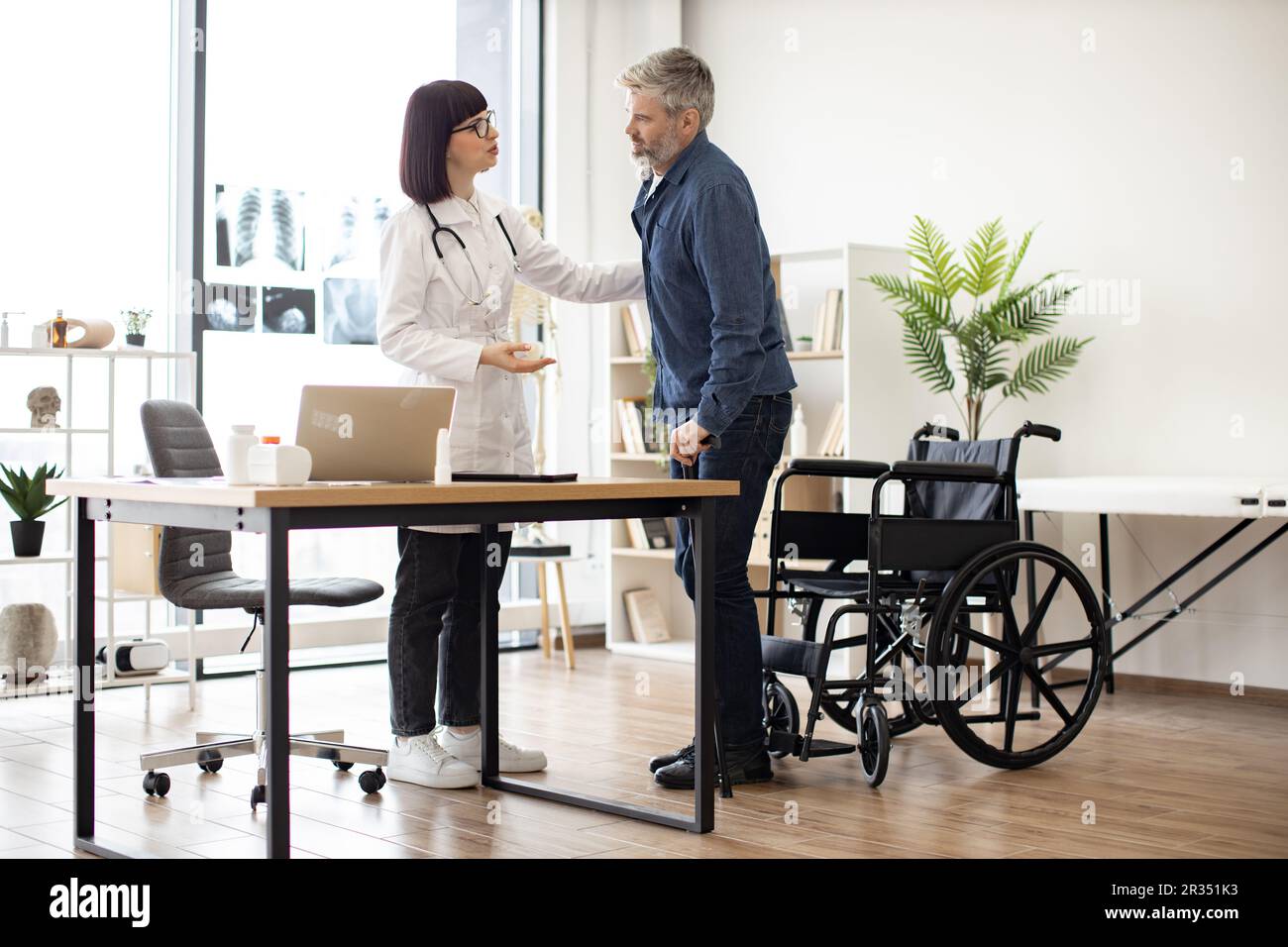 Full length view of man standing near wheelchair with cane while ...
