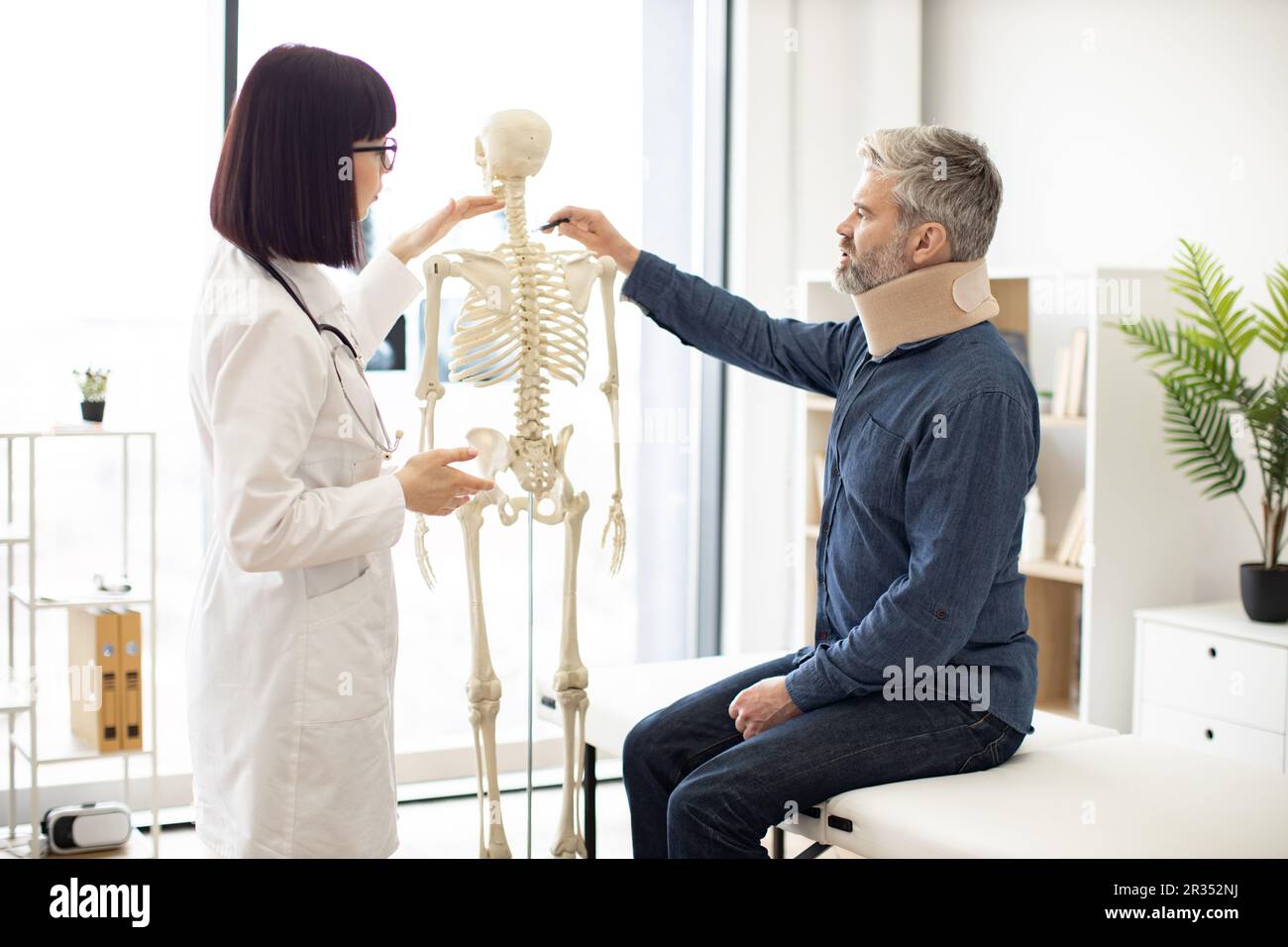 Focused brunette with stethoscope indicating on human skeleton while ...