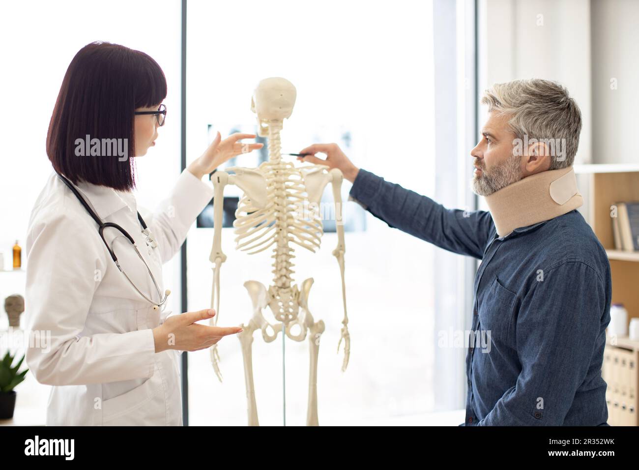 Focused brunette with stethoscope indicating on human skeleton while ...