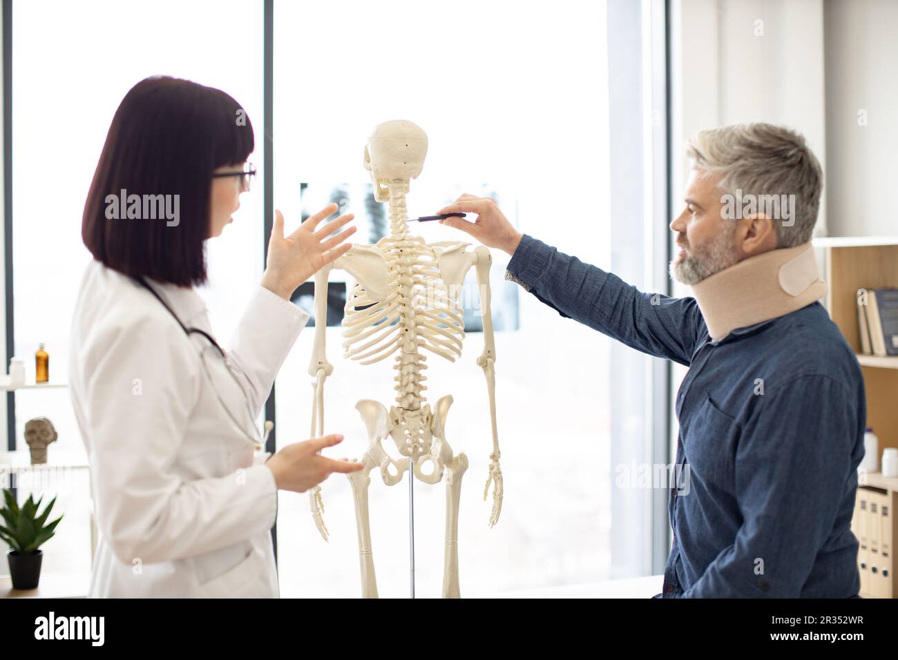 Focused brunette with stethoscope indicating on human skeleton while ...