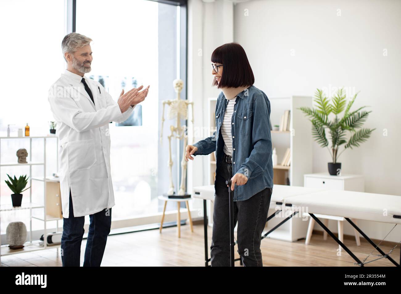 Cheerful doctor in white coat clapping hands while brunette lady in C ...