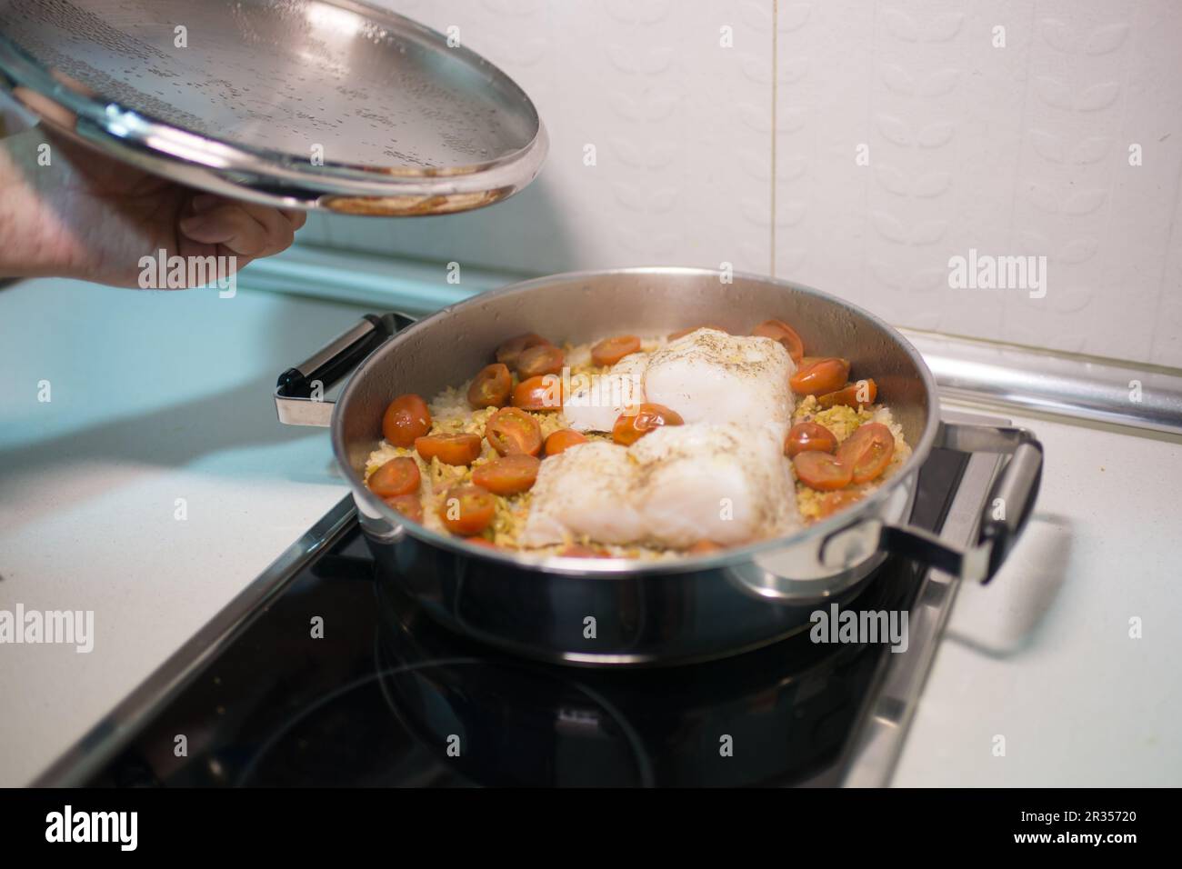 Human hand opening a cooking pot with rice, hake and cherry tomatoes ...