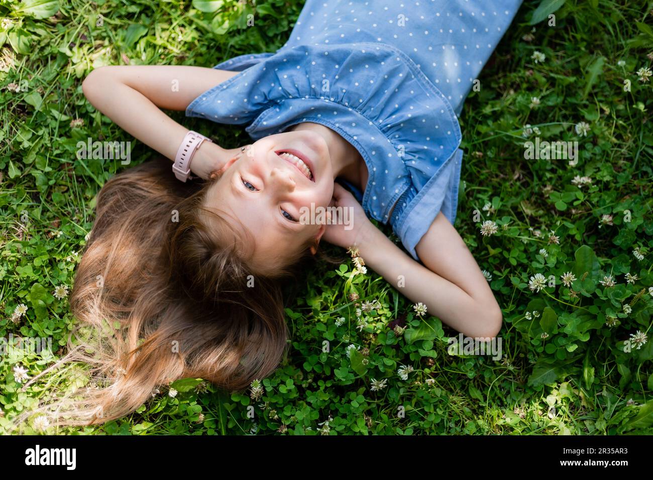 happy little girl lying on the green grass in summer top view. High ...