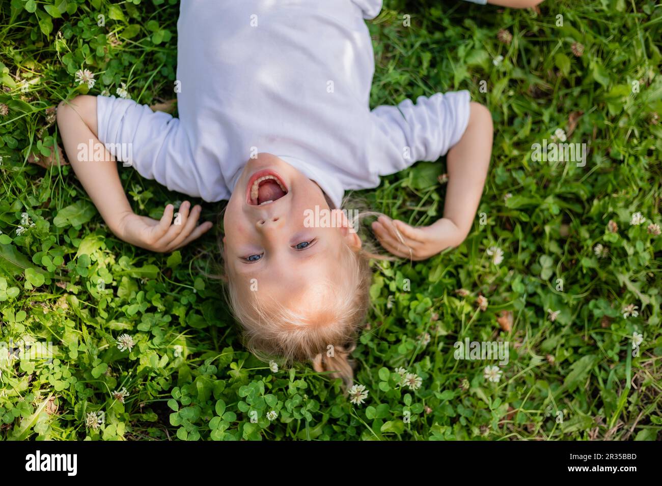 happy little boy lying on the green grass in summer top view in a white ...