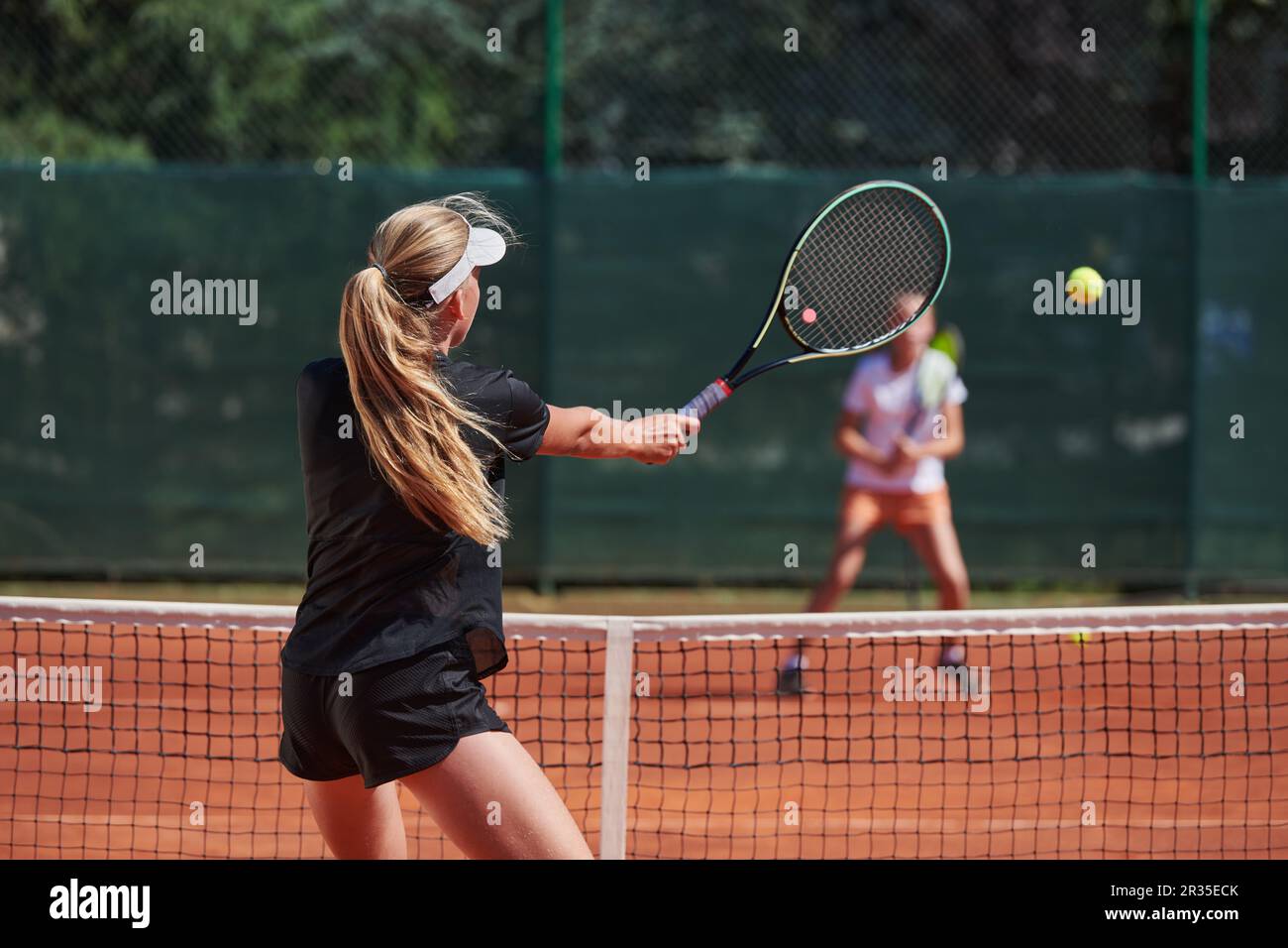 Young girls in a lively tennis match on a sunny day, demonstrating ...
