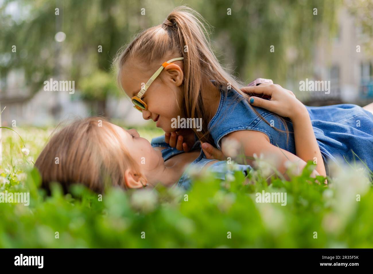 two happy little girls are playing lying on the green grass in summer ...