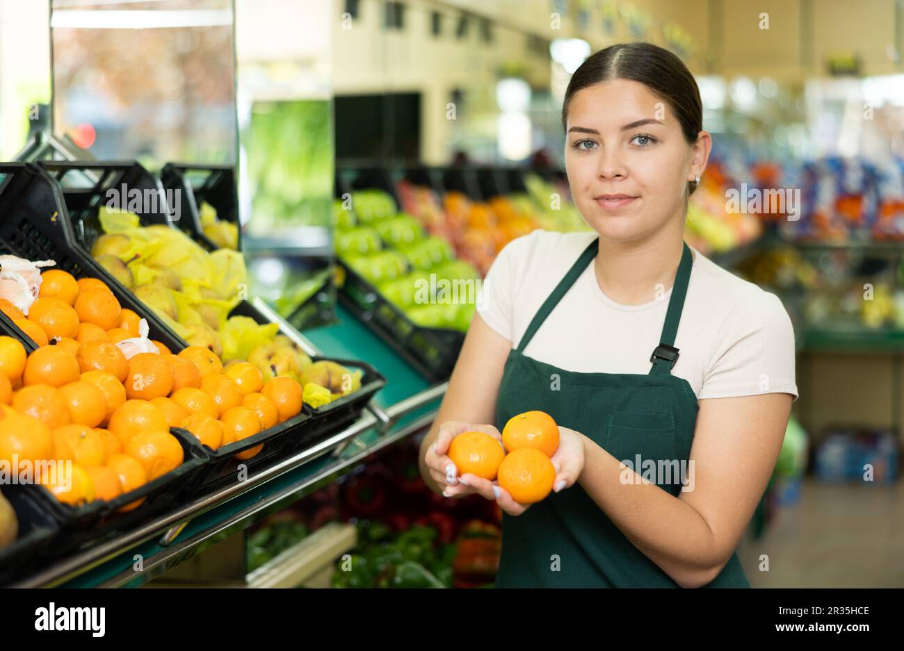 Female grocery store worker lays out ripe tangerines on counter and ...