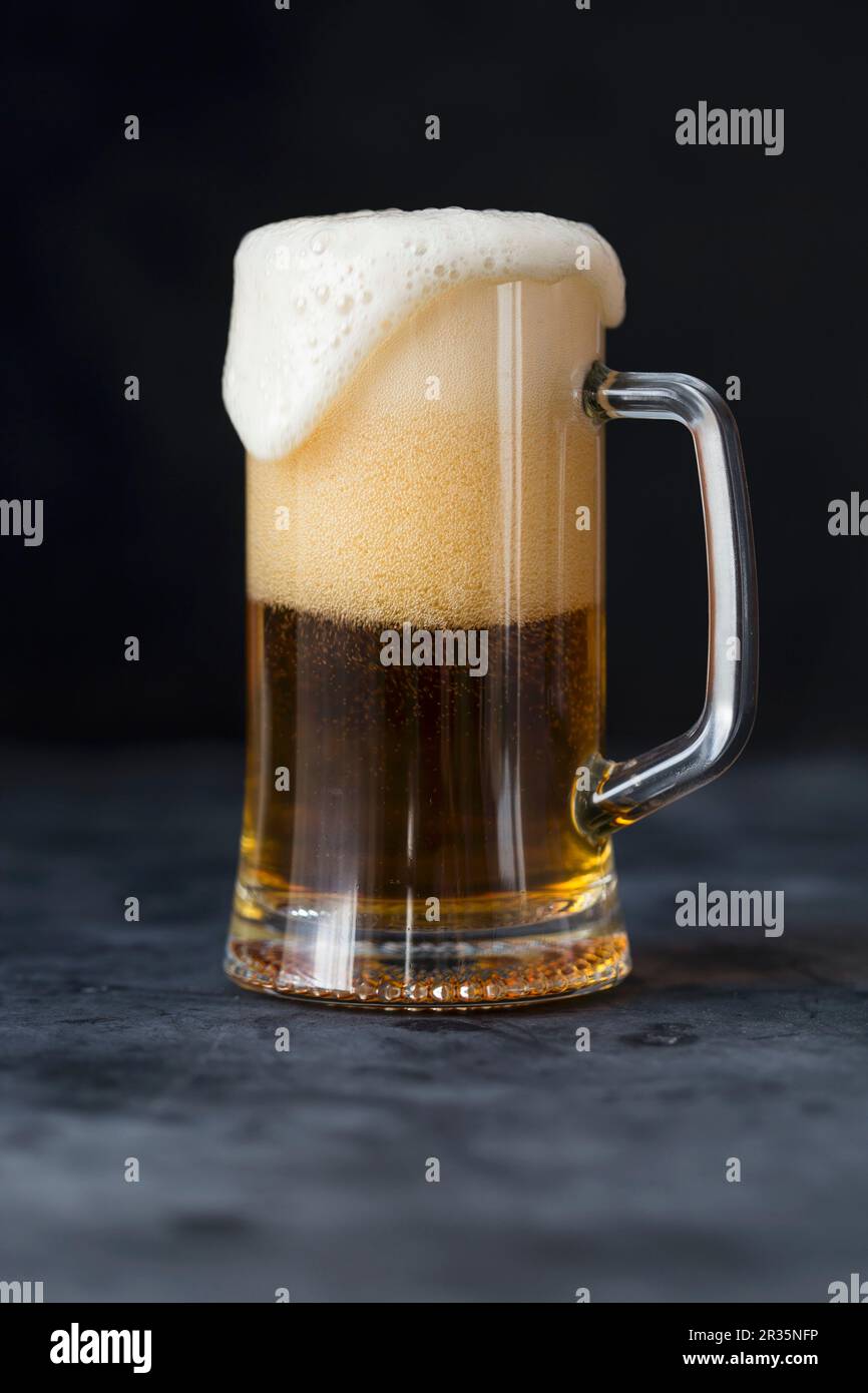 A glass of beer with overflowing foam Stock Photo - Alamy