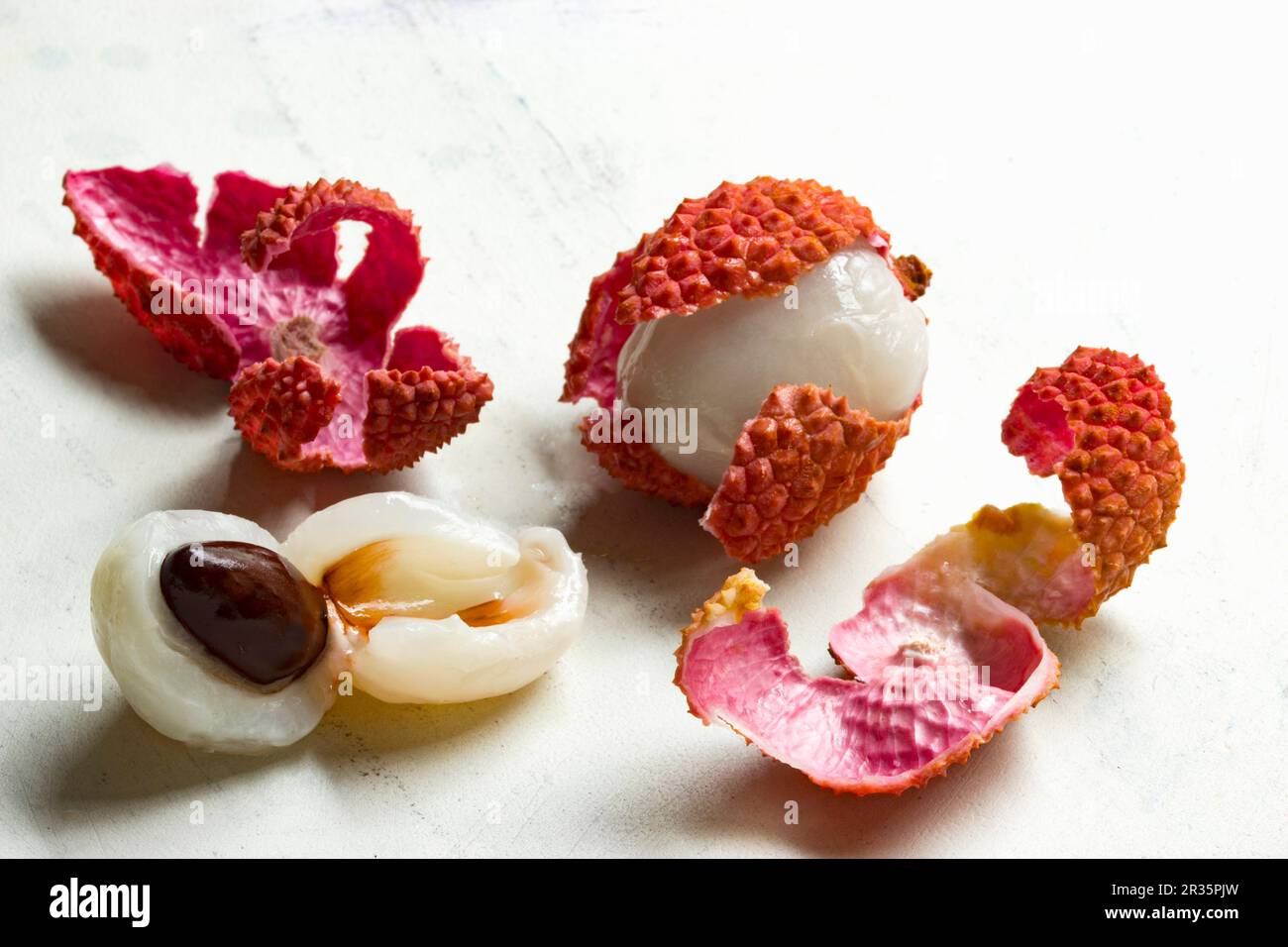 Lychees, peeled and opened with shells on a white surface Stock Photo ...