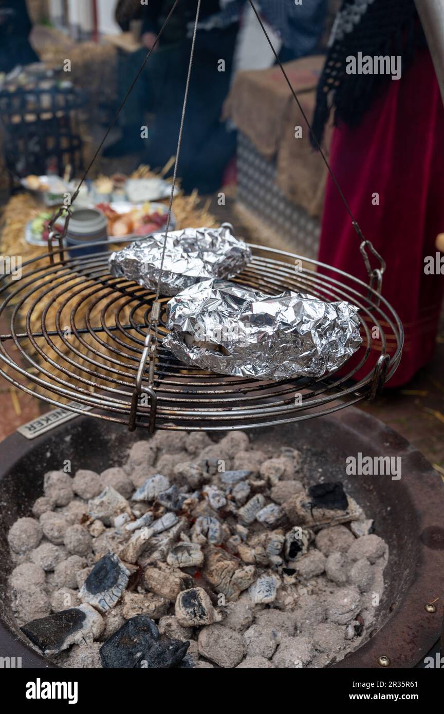 Potato in alumnium foil baked on charcoal barbecue grill outdoor in ...