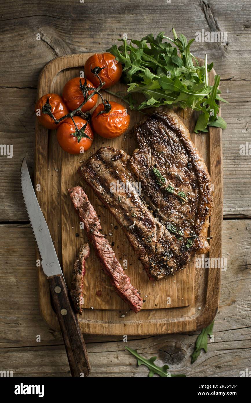 Grilled beef steak with tomatoes and rocket on a chopping board Stock ...