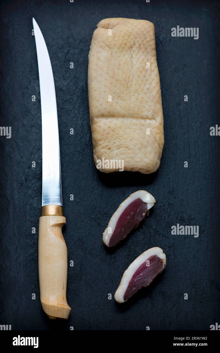 Smoked preserved duck breast with slices cut off next to a flitting ...