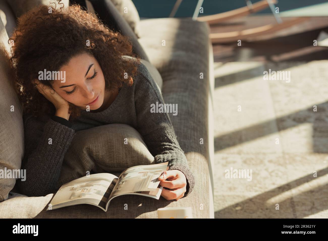 A relaxed young woman with curly hair lies belly-down on the couch in ...