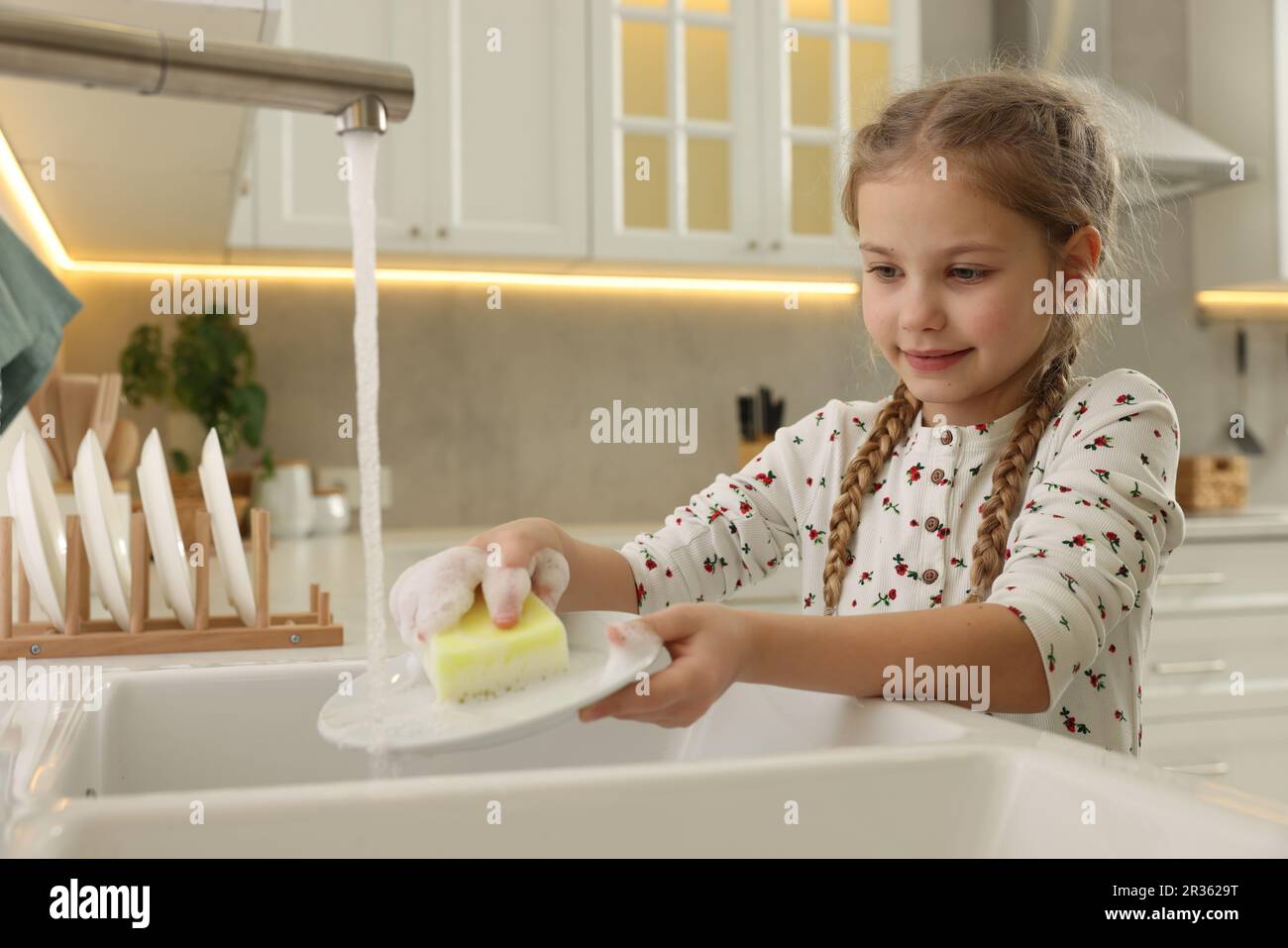 Little girl washing plate above sink in kitchen Stock Photo - Alamy