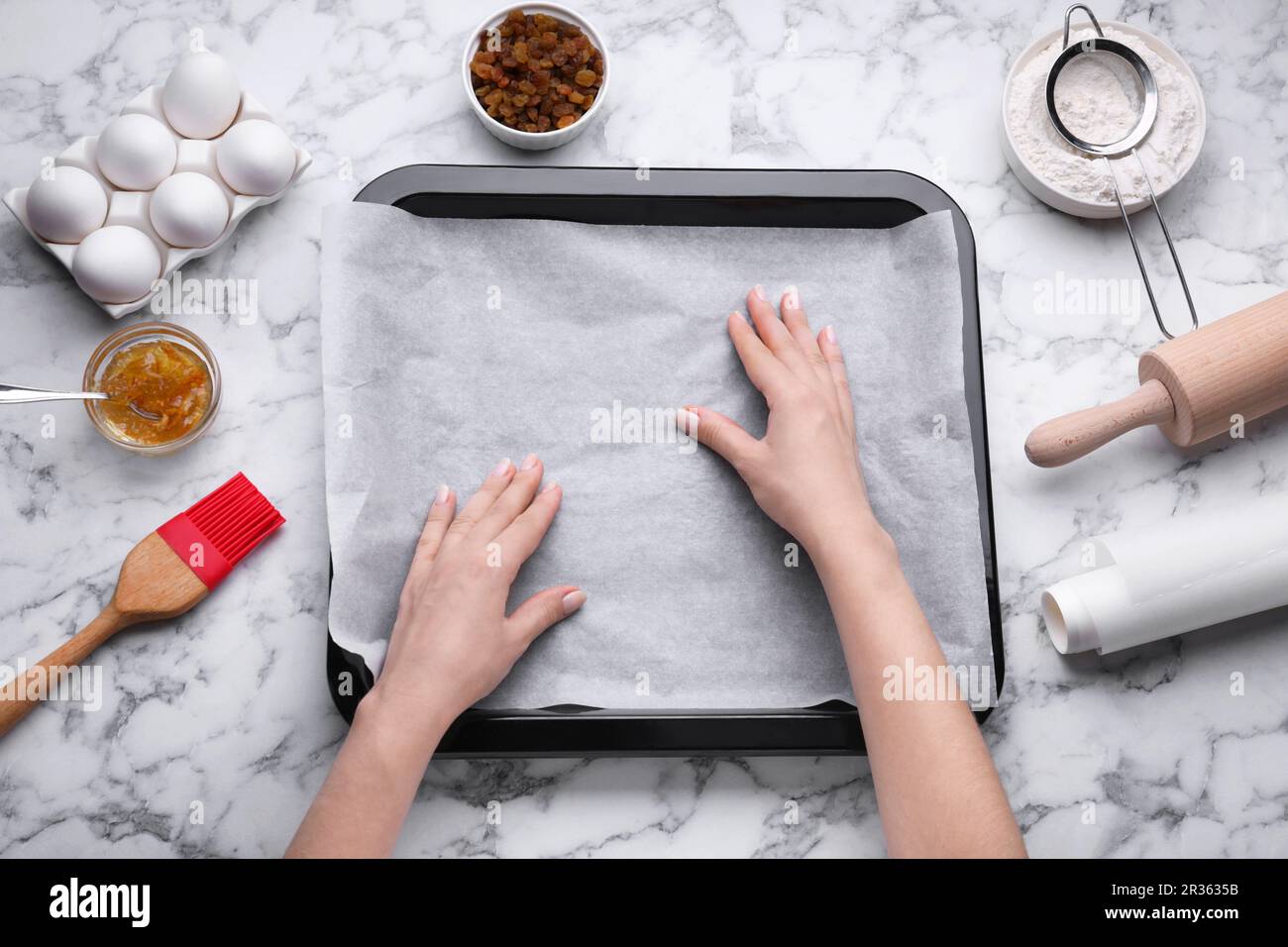 Woman putting parchment paper in baking pan at white marble table, top ...