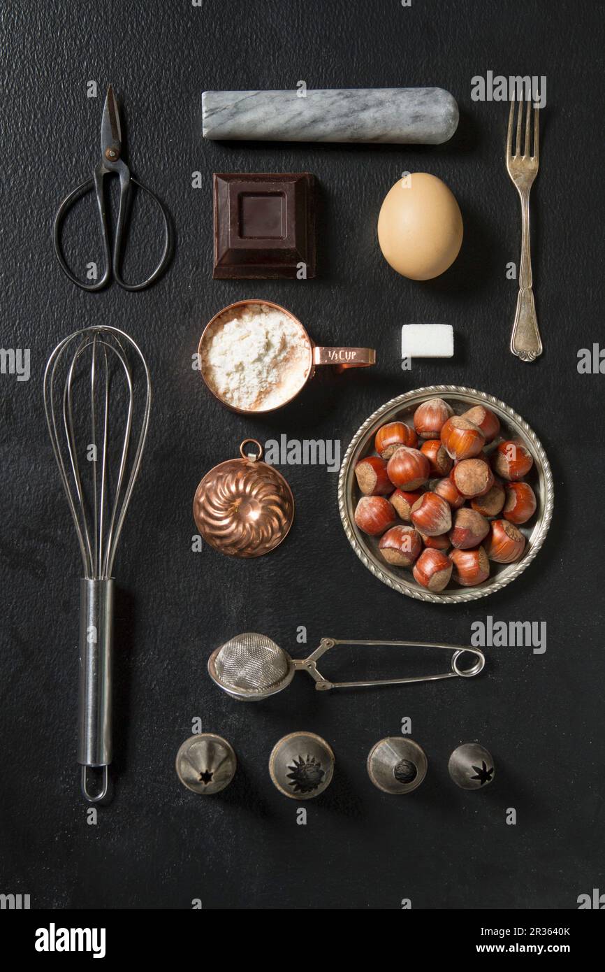 An arrangement of kitchen utensils and baking ingredients on a dark ...