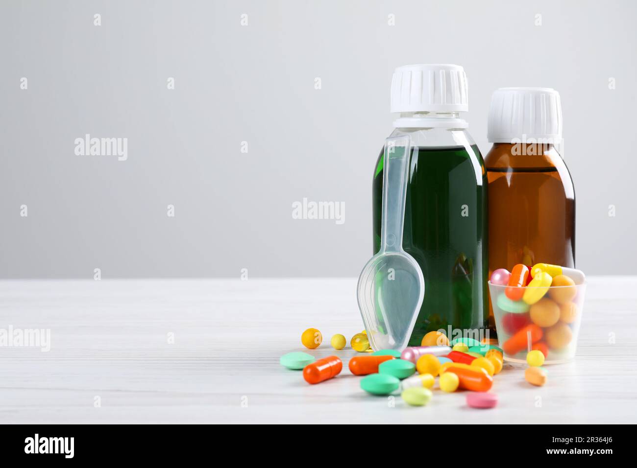 Bottles of syrups with pills on wooden table against white background ...