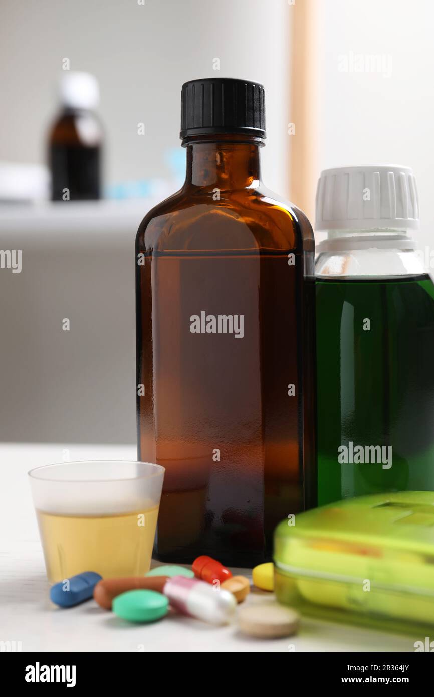 Bottles of syrup, measuring cup and pills on table. Cold medicine Stock ...
