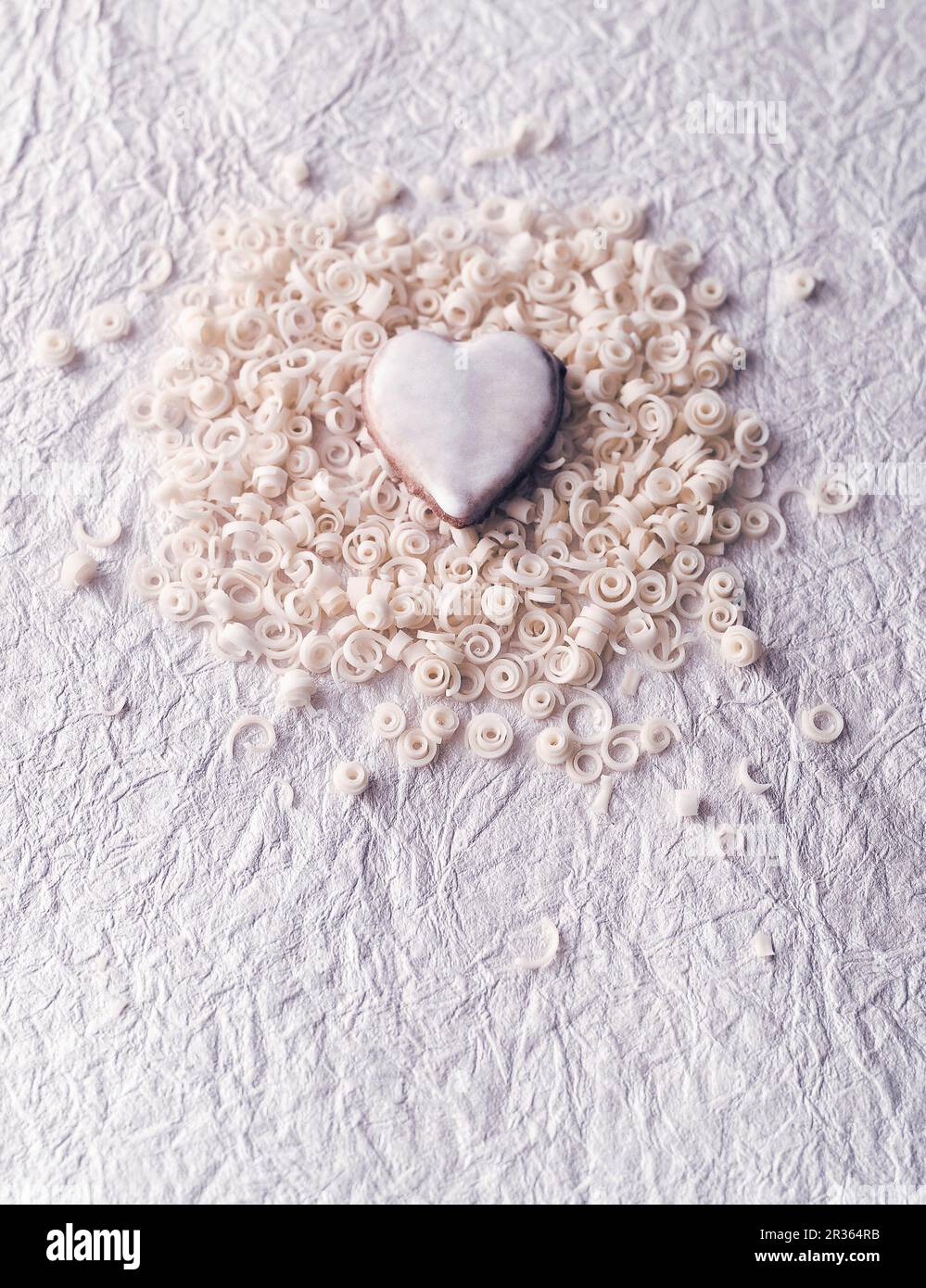 A heart-shaped biscuit with curls of white chocolate on a piece of ...
