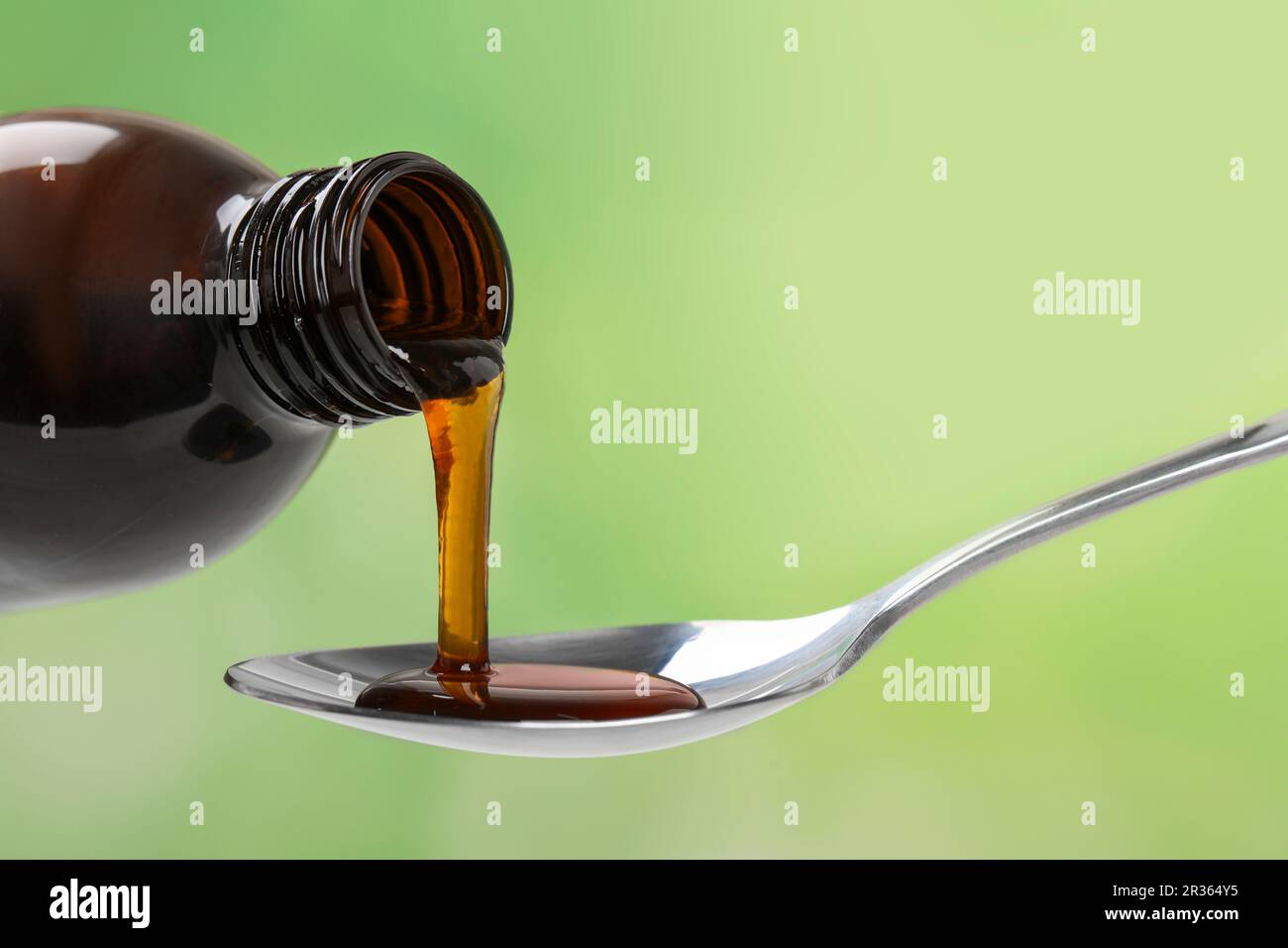 Pouring syrup from bottle into spoon against light green background ...