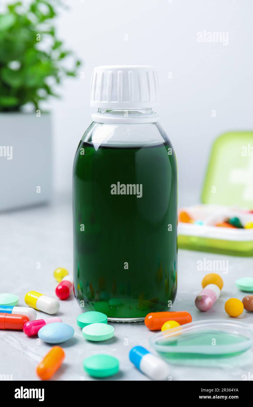 Bottle of syrup, dosing spoon and pills on white table. Cold medicine ...