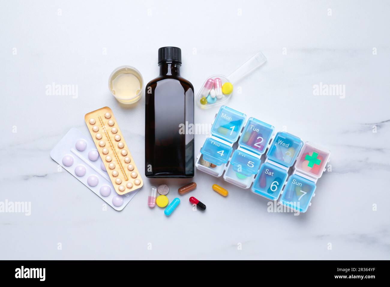 Bottle of syrup, measuring cup, dosing spoon and pills on white marble ...