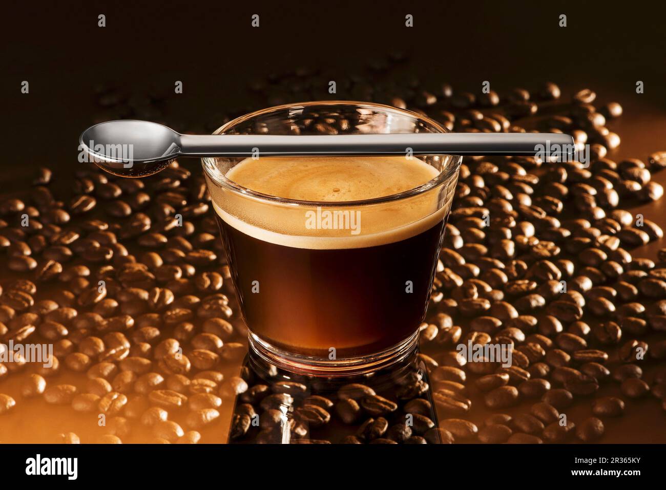 Glass of espresso with a spoon on a reflective surface with coffee ...