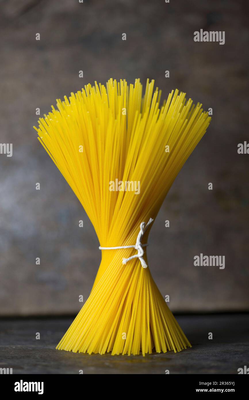 A bundle of spaghetti tied with string standing on a grey surface Stock ...
